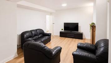 Uma sala de estar moderna com um sofá de couro preto, uma TV de tela plana sobre um suporte preto e piso de madeira.