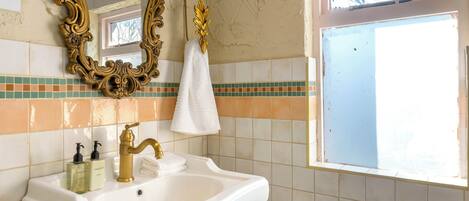 Uma casa de banho com lavatório branco, torneiras douradas e um espelho grande e ornamentado.