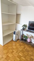 Quarto com radiador branco, televisão sobre suporte de madeira e um vaso de planta.