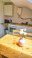 Uma cozinha com mesa de madeira, vaso com flores, cafeteira e torradeira.