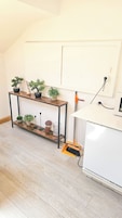 Quarto com uma escrivaninha branca, um aparador de madeira com plantas em vasos, um esfregão e uma lousa na parede.