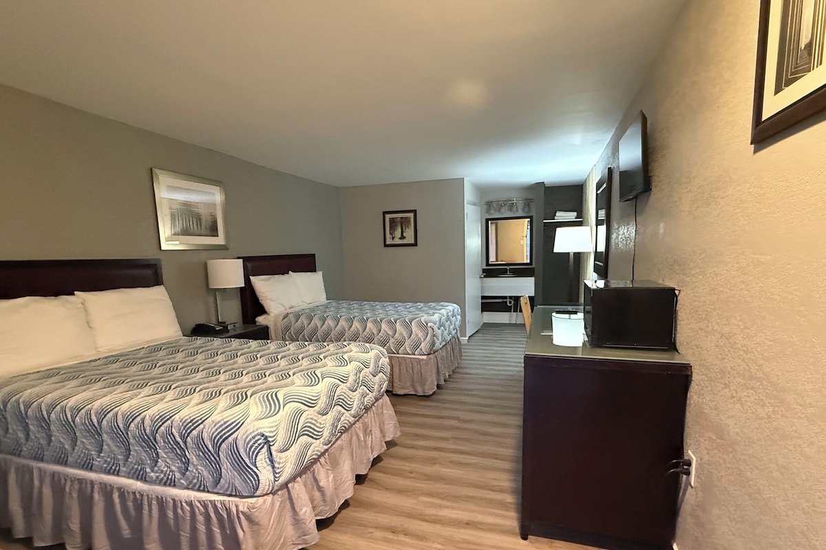 Quarto de hotel com duas camas, uma escrivaninha, uma televisão e um espelho.