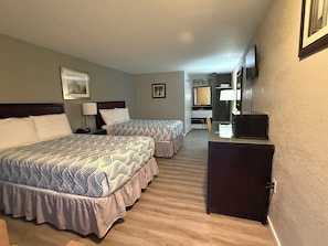 Quarto de hotel com duas camas, uma escrivaninha, uma televisão e um espelho.