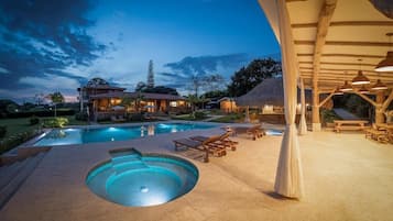 Piscina com espreguiçadeiras e área coberta, cercada por edifícios e árvores.