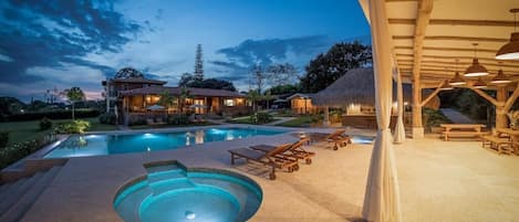 Piscina com espreguiçadeiras e área coberta, cercada por edifícios e árvores.