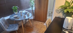 Uma área de refeições compacta com mesa redonda, duas cadeiras, cafeteira e plantas em vasos.