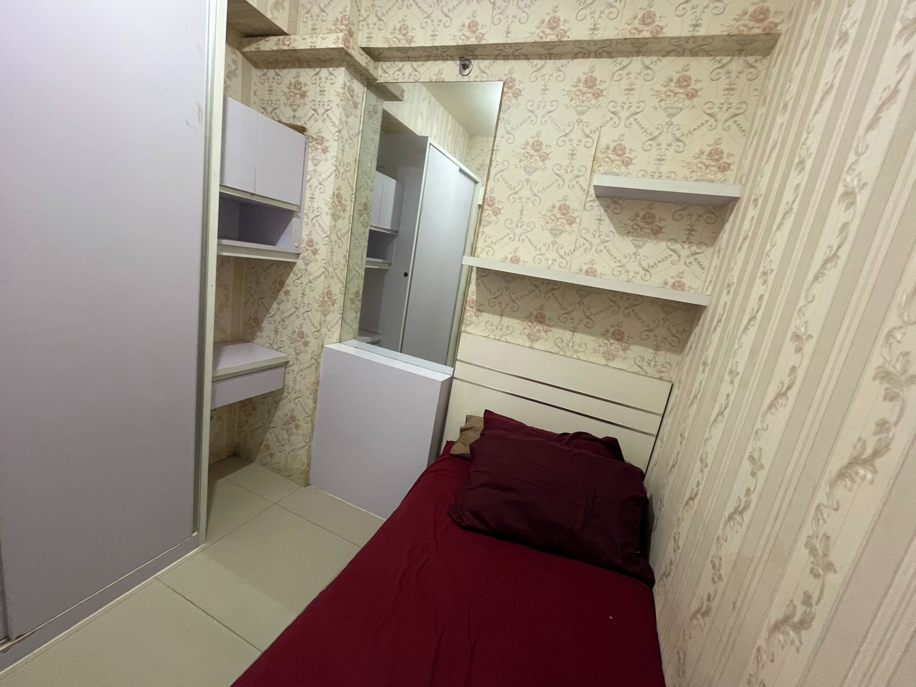 Quarto pequeno com uma cama de solteiro, guarda-roupa e espelho.