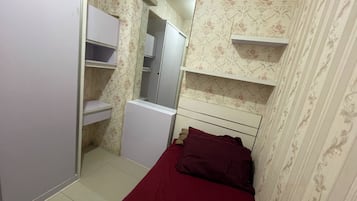 Quarto pequeno com uma cama de solteiro, guarda-roupa e espelho.