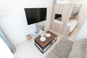 Quarto de hotel compacto com TV de tela plana, uma pequena mesa de escritório com computador, mesa de jantar para dois, beliche e sofá.