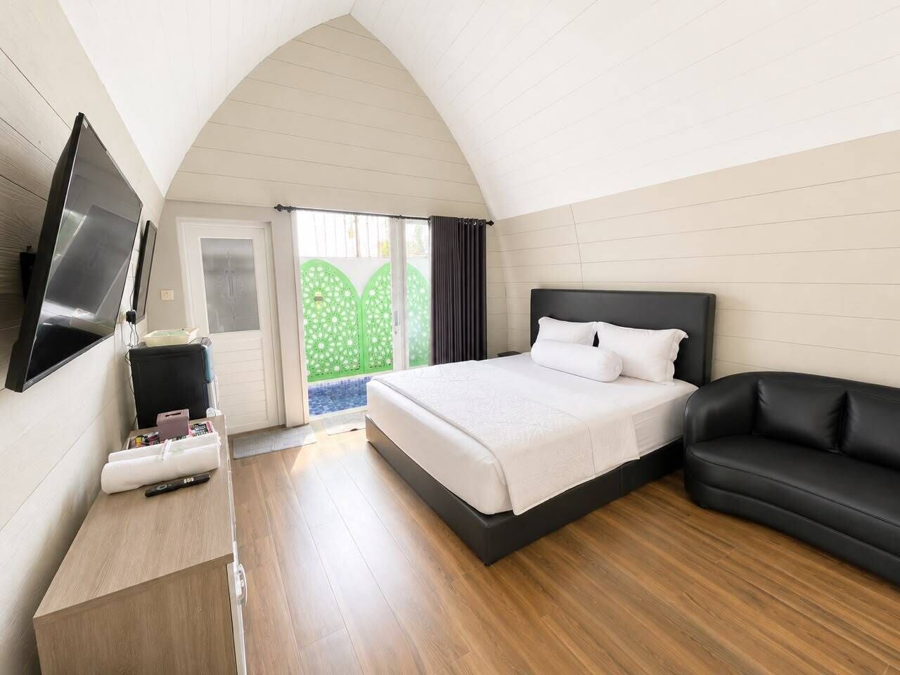 Quarto moderno com cama, sofá preto, televisão e escrivaninha com cadeira.