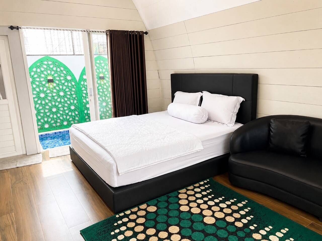Quarto com cama, sofá de couro preto, tapete estampado e parede decorativa verde.