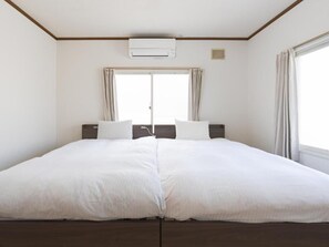 Uma cama de casal com cabeceira, uma janela com cortinas e um aparelho de ar condicionado na parede.