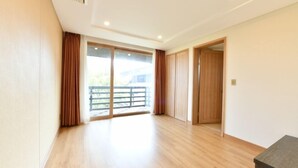 Um quarto espaçoso com piso de madeira, grandes portas de vidro deslizantes que dão para uma varanda e uma porta de madeira.