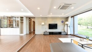 Uma sala de estar moderna com televisão de tela plana, um sofá, uma mesa de centro e uma grande janela com vista para o exterior.