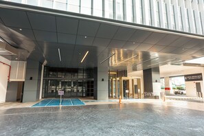 Entrada de um edifício moderno com fachada de vidro, um letreiro para Mitsui Serviced Suites e o logotipo SWNK.