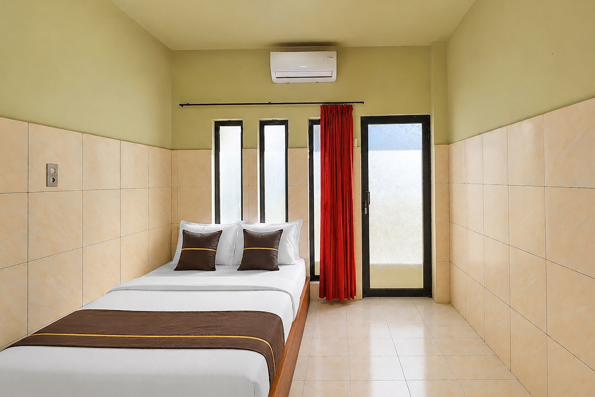 Quarto de hotel com cama, janela com cortinas, ar condicionado e piso ladrilhado.