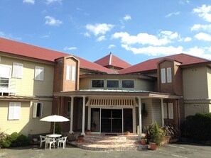 Um hotel com varanda coberta, entrada central e estrutura em dois andares.