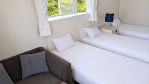 Quarto com duas camas, um sofá, uma luminária e uma janela com cortinas.
