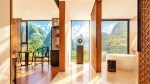 Um banheiro moderno com uma banheira grande, uma cadeira de madeira e uma mesa com vista para uma paisagem montanhosa.