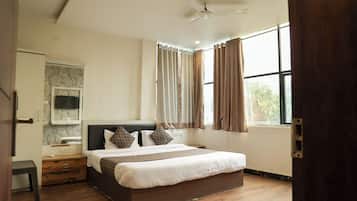 Quarto com cama, mesa de cabeceira, penteadeira, ventilador de teto e janela com cortinas.