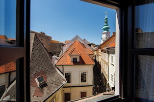 Visão de um edifício com telhado de telhas vermelhas e um pináculo verde, visto através de uma janela.