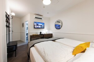 Quarto de hotel com cama, escrivaninha, televisão e espelho.