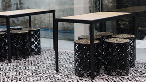 Um interior moderno com mesas e cadeiras de metal preto, ladrilhos estampados e um painel de vidro.