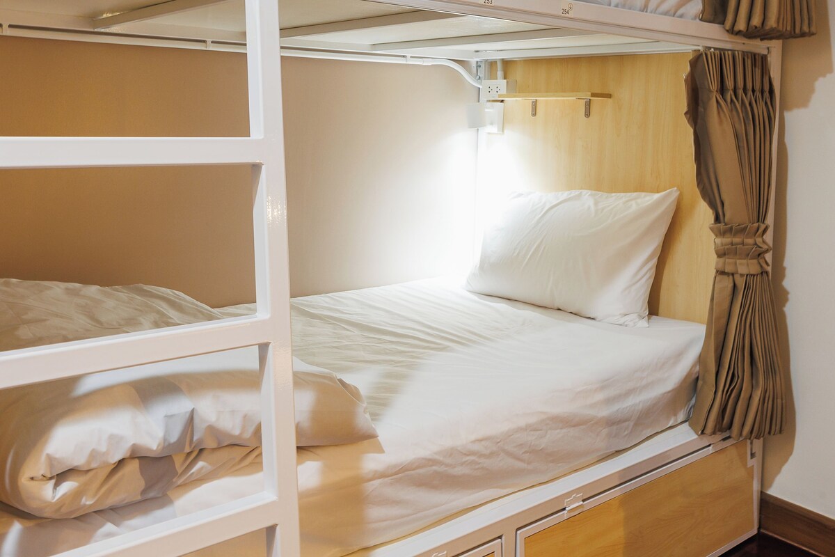 Uma cama beliche com estrutura de madeira, roupa de cama branca e uma cortina no lado direito.