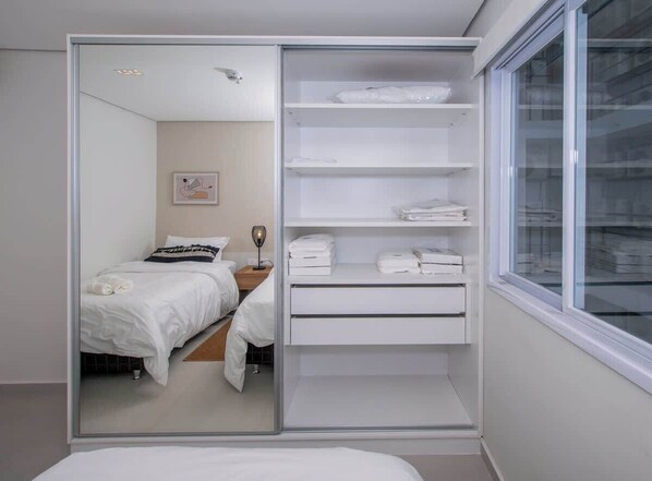 Quarto com cama, mesa de cabeceira, espelho e guarda-roupa com prateleiras.