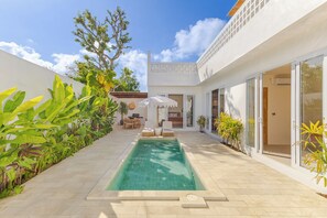 Uma área de piscina moderna, com piscina translúcida, rodeada por plantas e um terraço com assentos.