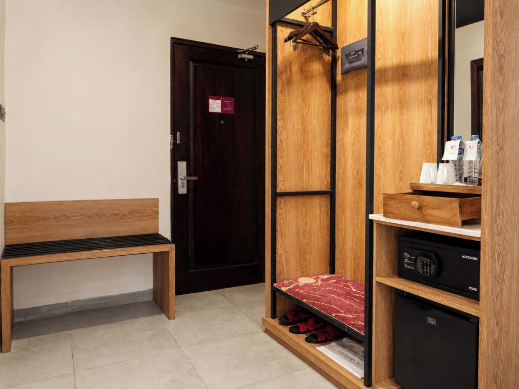 Quarto de hotel com um banco de madeira, um guarda-roupa com espelho e uma prateleira com produtos de higiene pessoal.