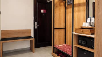 Quarto de hotel com um banco de madeira, um guarda-roupa com espelho e uma prateleira com produtos de higiene pessoal.