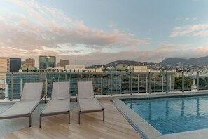Área de piscina no terraço com espreguiçadeiras e vista para a cidade.