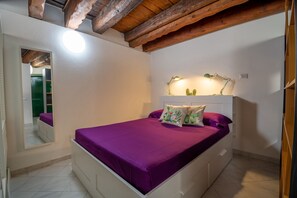 Quarto com cama, mesa de cabeceira, espelho e teto com vigas aparentes.
