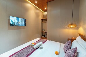 Quarto de hotel com uma cama, televisão fixada na parede, guarda-roupa, mesa de cabeceira e luminária suspensa.