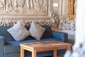 Um quarto com um sofá azul, duas almofadas cinzas e uma mesa de centro de madeira.