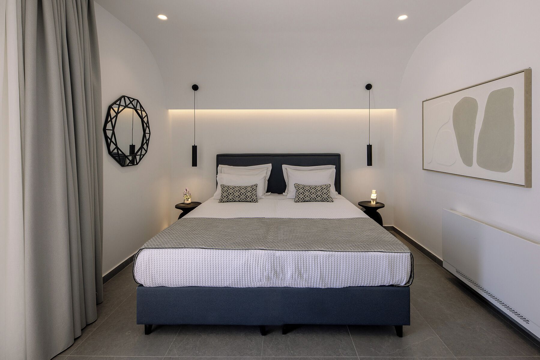 Quarto moderno com uma cama grande, mesas de cabeceira, luminária fixada na parede e um quadro abstrato emoldurado.