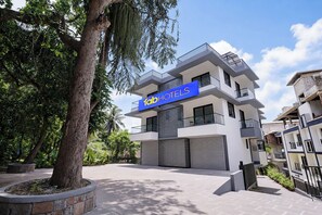 Um hotel moderno de vários andares com um letreiro azul chamativo, varandas e uma área de entrada pavimentada.