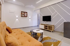 Uma sala de estar moderna com um sofá, uma mesa redonda pequena, uma televisão fixada na parede e um armário abaixo.