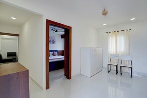 Quarto de hotel com cama, escrivaninha, cadeira, guarda-roupa e ventoinha no teto.