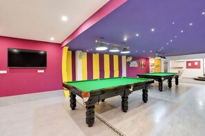 Uma área de jogos com duas mesas de bilhar, uma TV de tela plana e uma placa indicando 'Game Lounge'.