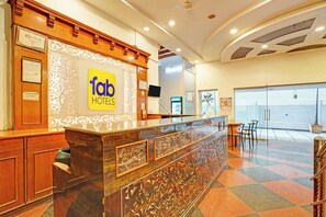 Uma área de recepção de hotel com um balcão de madeira, divisória de vidro e uma janela grande.
