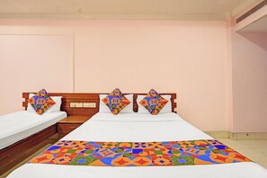 Quarto de hotel com cama, duas almofadas, mesa de cabeceira e parede com interruptor de luz.