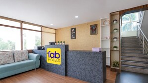 Área de recepção de hotel com um sofá, balcão de atendimento, escada e uma parede com quadros emoldurados.