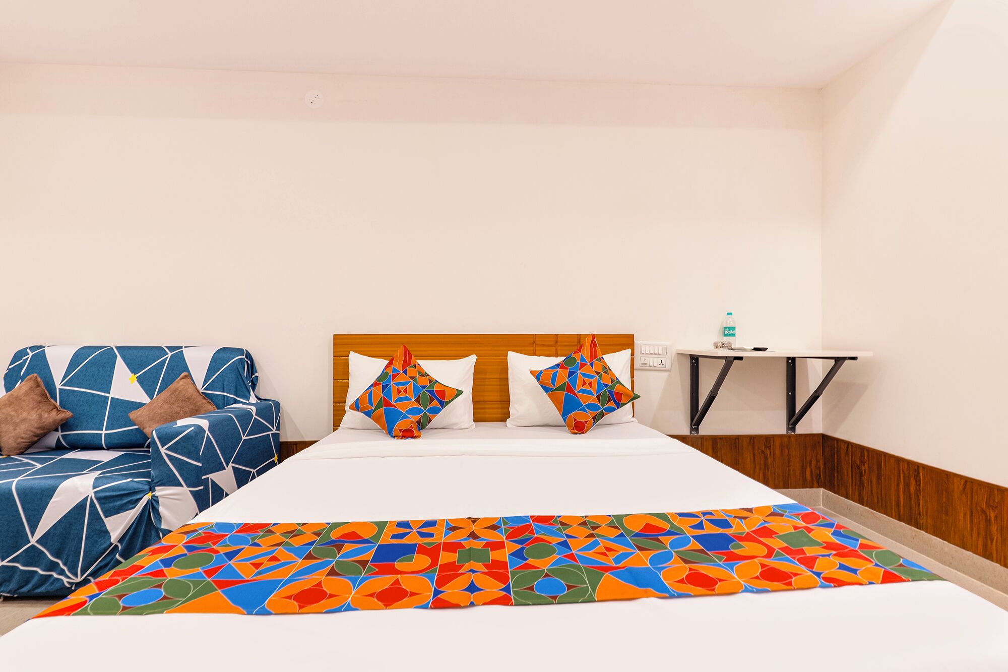 Quarto de hotel com cama, sofá, uma mesinha e uma tomada.