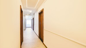 Um corredor comprido e estreito com portas de madeira em ambos os lados, que leva a um quarto claro no final.
