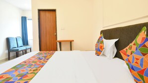 Quarto de hotel com cama, uma cadeira, escrivaninha e porta.