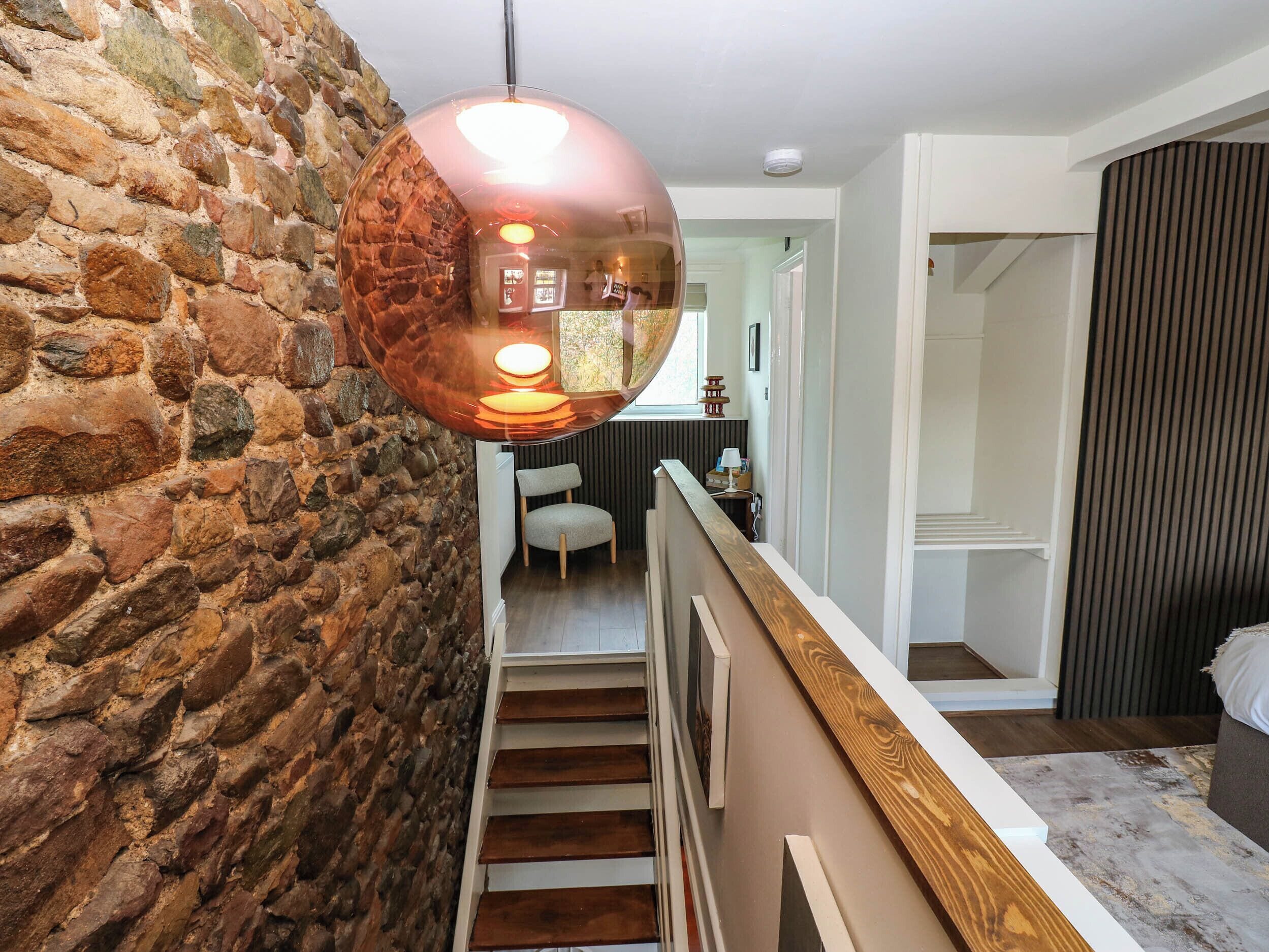 A staircase with a wooden handrail, a stone wall, and a hanging light fixture.