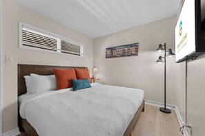 Quarto de hotel com cama, televisão, obra de arte na parede e abajur.