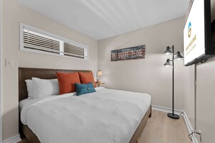 Quarto de hotel com cama, televisão, obra de arte na parede e abajur.